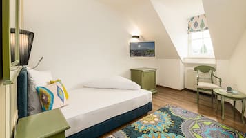 Quarto com cama, um armário verde, uma cadeira, uma mesinha e uma janela com vista para a paisagem urbana.