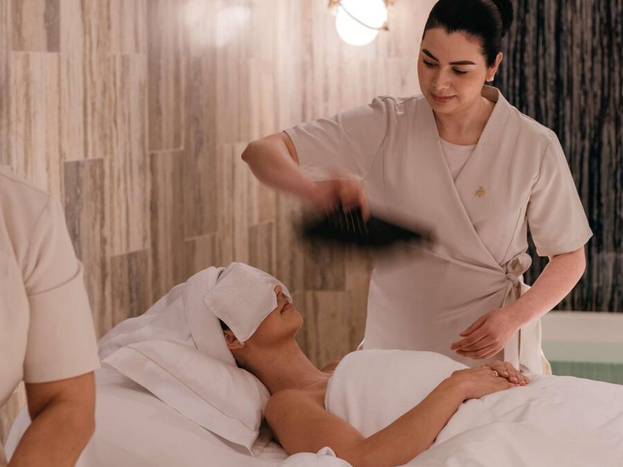 Uma pessoa recebe tratamento facial em um quarto com painéis de madeira e luminária.