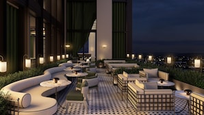Terraço no topo com mobiliário externo, iluminação suave e vista da cidade ao entardecer.
