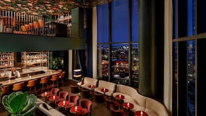 Uma área de bar com vista para a cidade, assentos com detalhes em vermelho e uma planta.