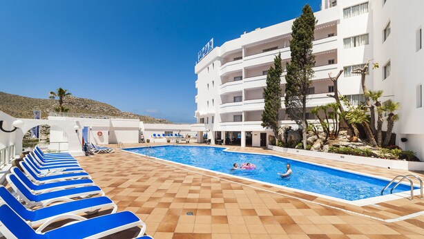 Uma área de piscina com cadeiras de descanso azuis, uma piscina e um edifício com uma placa.