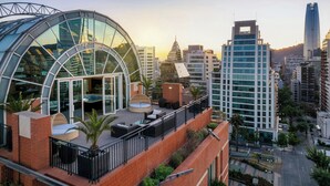 Um terraço moderno no telhado com paredes de vidro, área de estar externa e vista para a cidade.