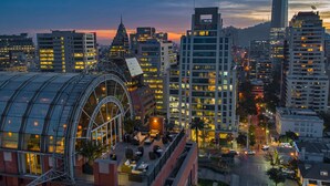 Um edifício alto com vários andares, janelas amplas e um terraço no telhado com área de estar ao ar livre.