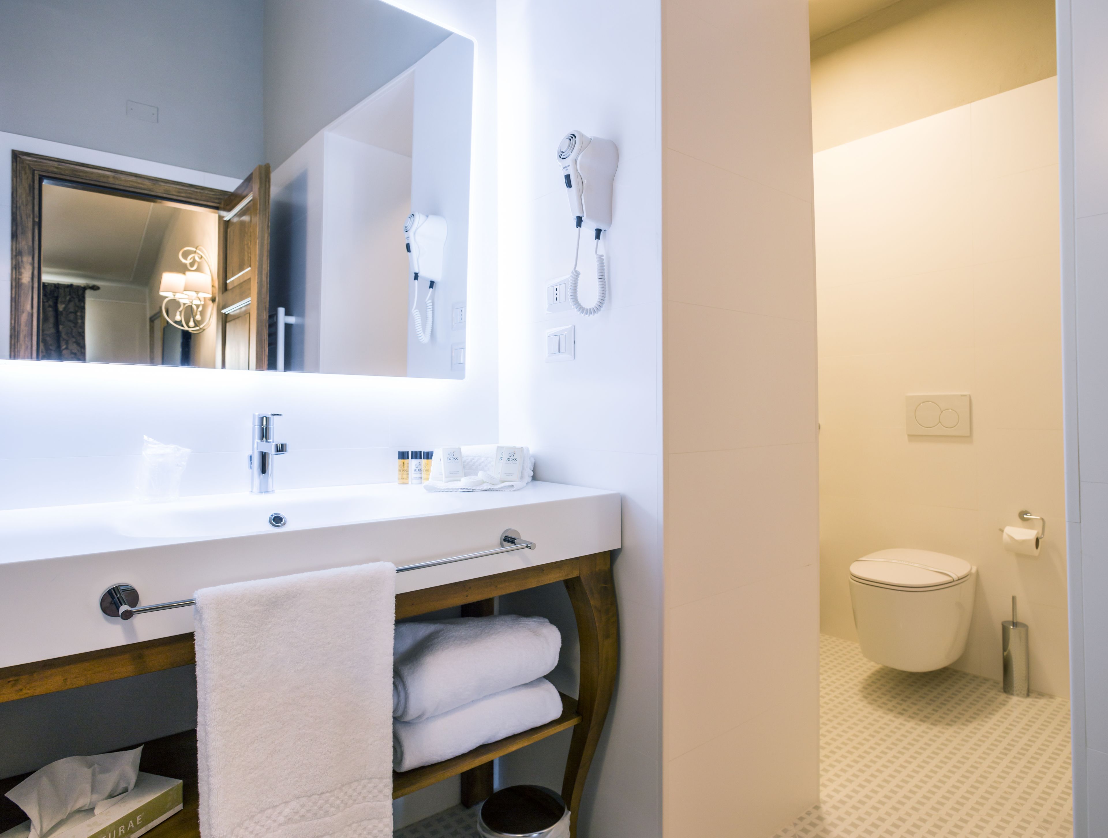 Casa de banho moderna com um espelho grande, lavatório branco e um secador de cabelo fixado na parede.