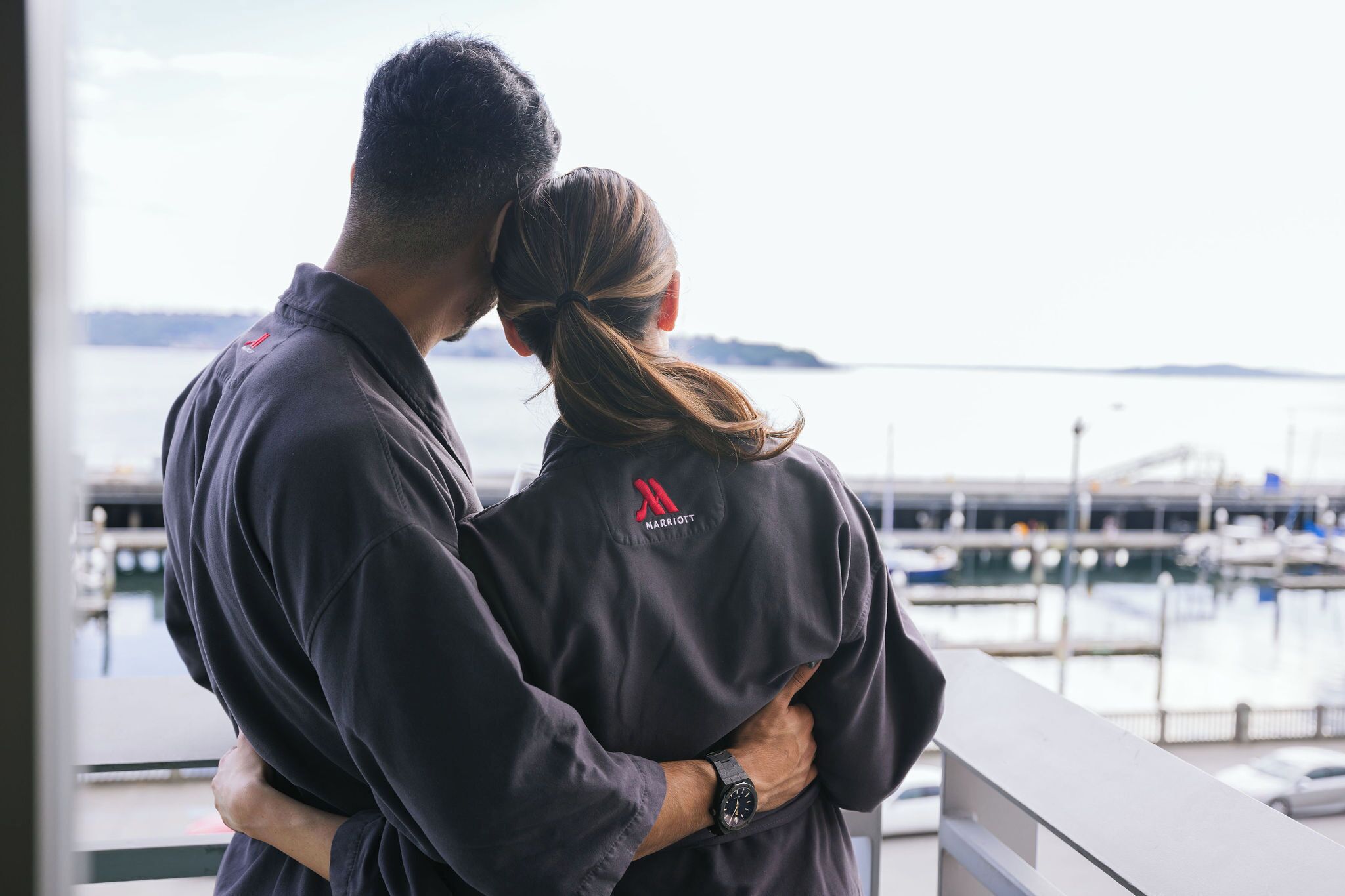 Um casal se abraçando em frente a um calhavete com barcos e uma linha de costa distante.