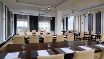 Sala de conferência com várias mesas, cadeiras e luminárias esféricas penduradas.
