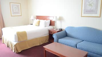 Quarto de hotel com uma cama, um sofá azul, uma mesa de cabeceira de madeira e uma mesa.