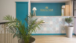 Uma área de recepção com parede cor de verde-água, painel de azulejos estampados e uma planta em vaso.