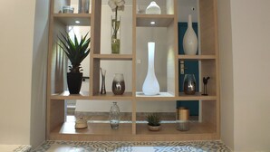Uma estante de madeira com diversos objetos decorativos, incluindo vasos, uma planta em vaso e uma pequena mesa com toalha estampada.