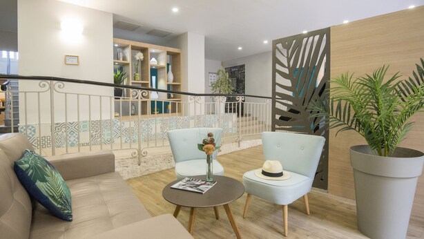 Um lobby moderno com um sofá bege, duas poltronas azul claro, uma mesa de centro redonda e uma grande planta em vaso.