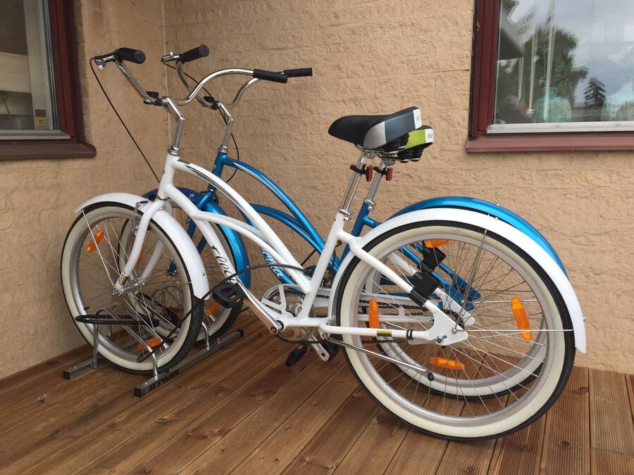 Uma bicicleta branca e azul encostada a uma parede, com uma janela ao fundo.