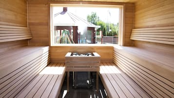 Uma sauna com bancos de madeira e uma mesa de pedra, janelas amplas e vista para um edifício lá fora.