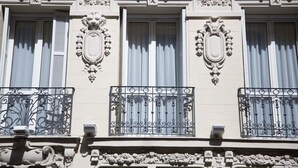 Fachada de edifício com detalhes arquitetônicos ornamentados, incluindo molduras decorativas e grades de varanda em ferro forjado.