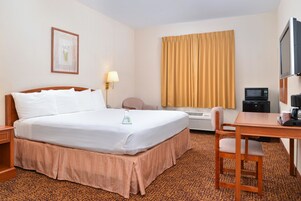 Quarto de hotel com cama, escrivaninha, cadeira, televisão e micro-ondas.