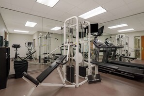 Uma academia com diversos equipamentos de exercício, incluindo esteiras, aparelhos de musculação e uma máquina de supino.