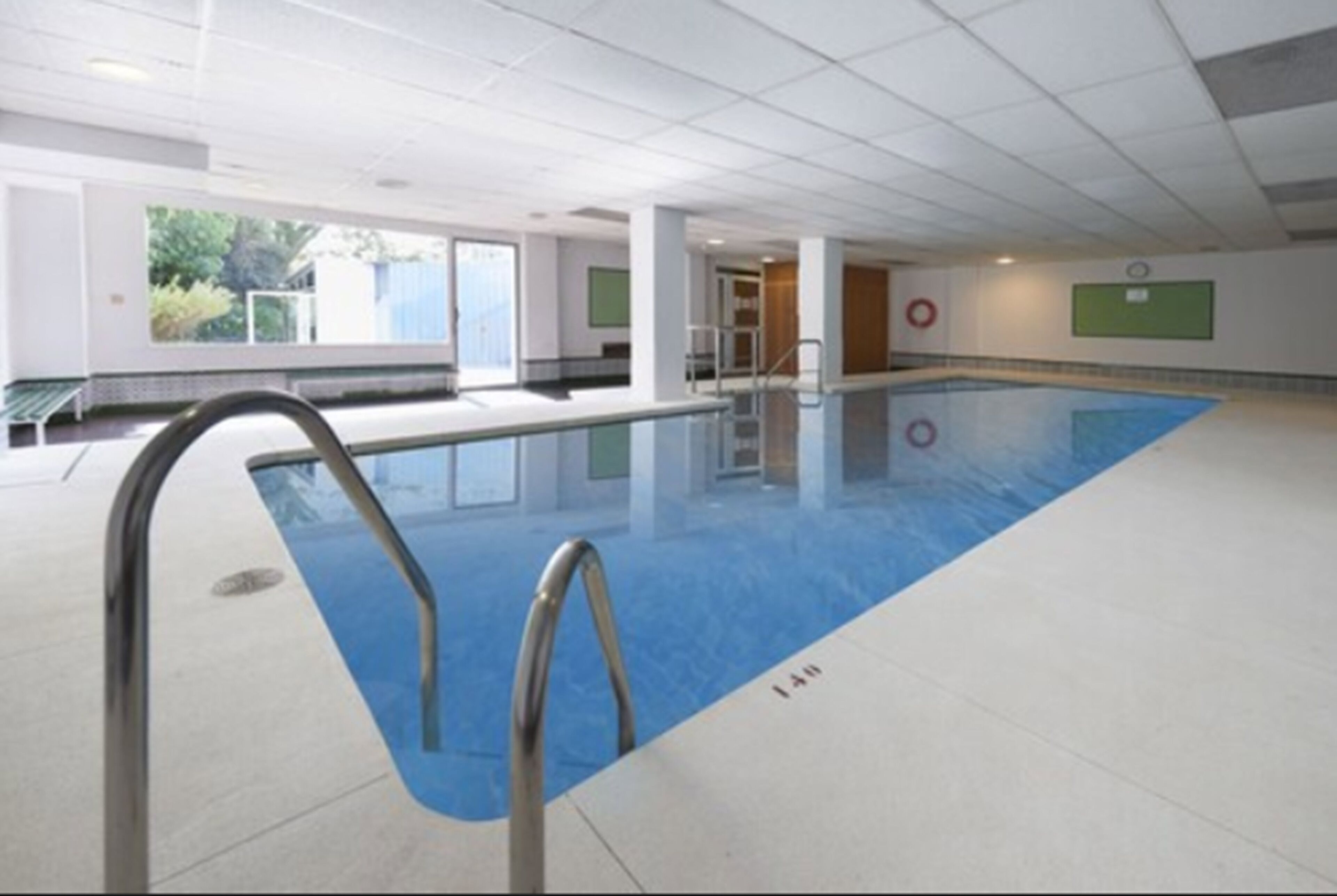 Piscina com água azul cristalina, escada de metal e chão revestido com azulejos.