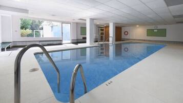 Piscina com água azul cristalina, escada de metal e chão revestido com azulejos.