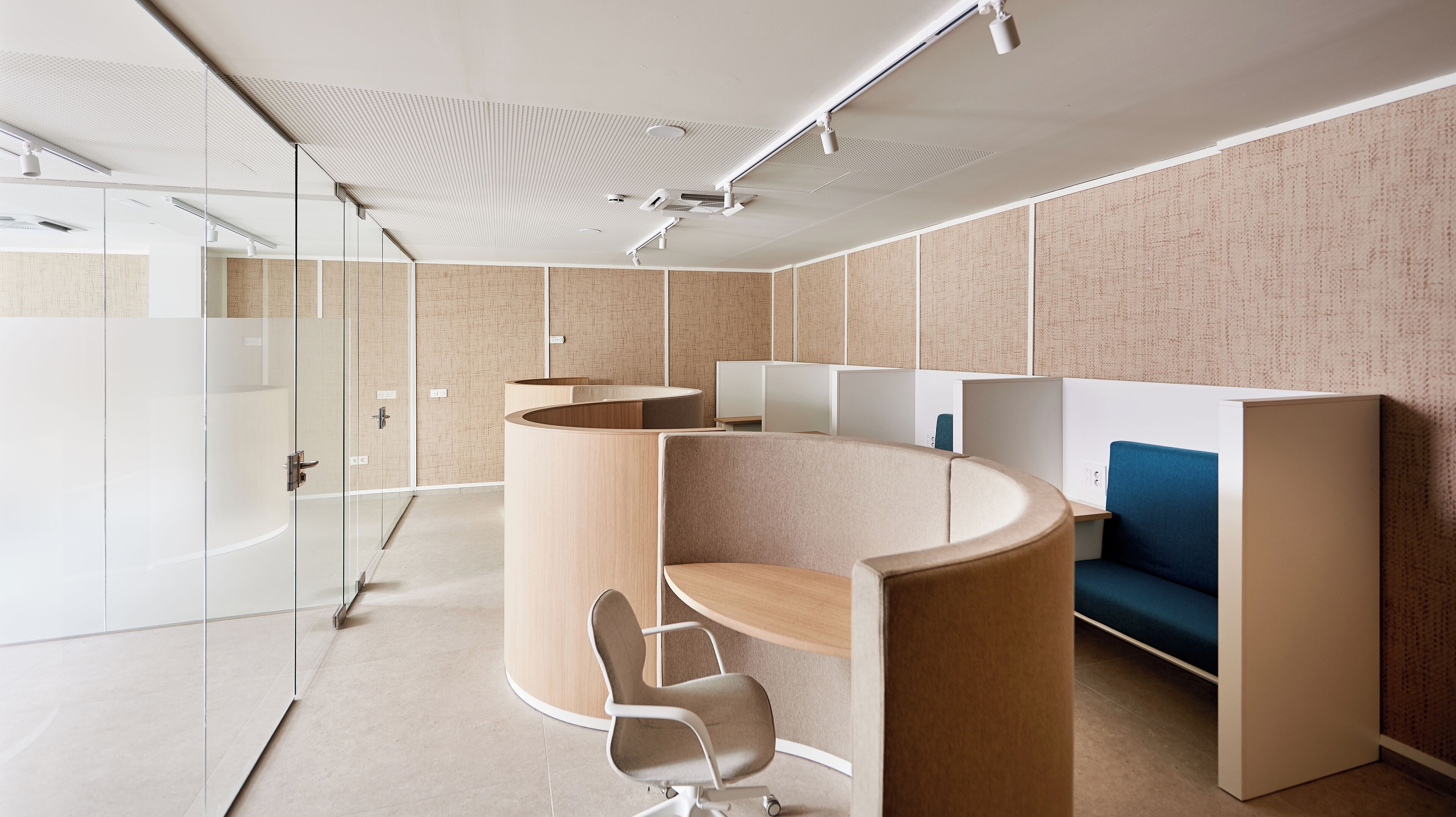 Um espaço de escritório moderno, com cubículos, uma mesa redonda e um sofá azul.