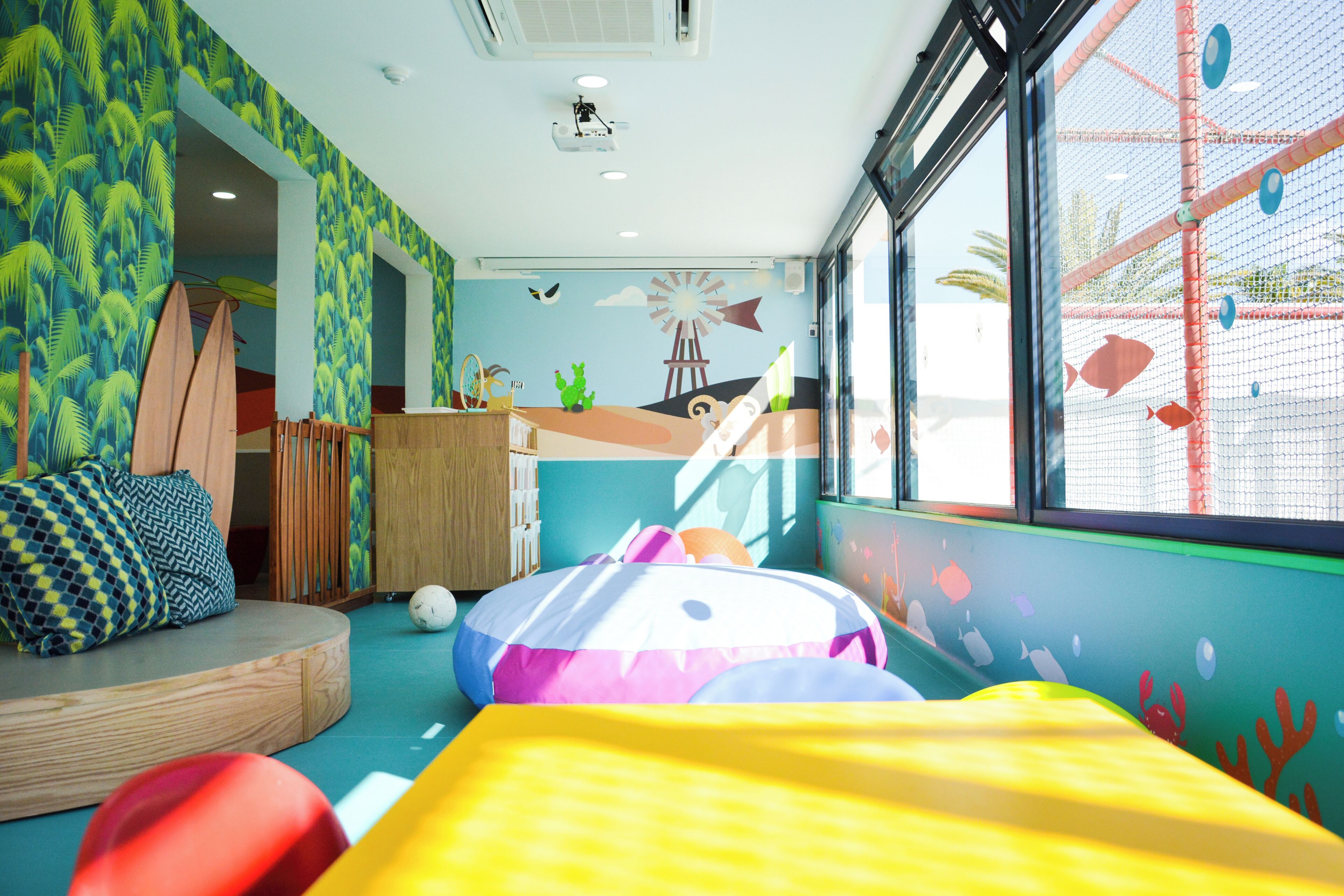 Quarto com mural, janela com vista e área de recreação com brinquedos.