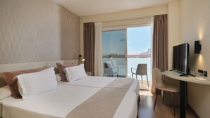 Quarto de hotel com uma cama grande, uma mesa de trabalho com televisão e uma varanda com vista.