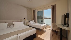 Quarto de hotel com duas camas, uma escrivaninha, uma cadeira, uma televisão e varanda com vista.