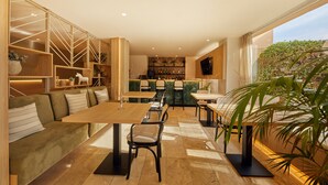 Uma área de jantar moderna com uma mesa e cadeiras de madeira, um sofá com almofadas e uma cozinha ao fundo.