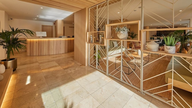 Uma área de recepção moderna com balcão de madeira, divisória de vidro e um espaço de estar com sofá e mesa de centro.