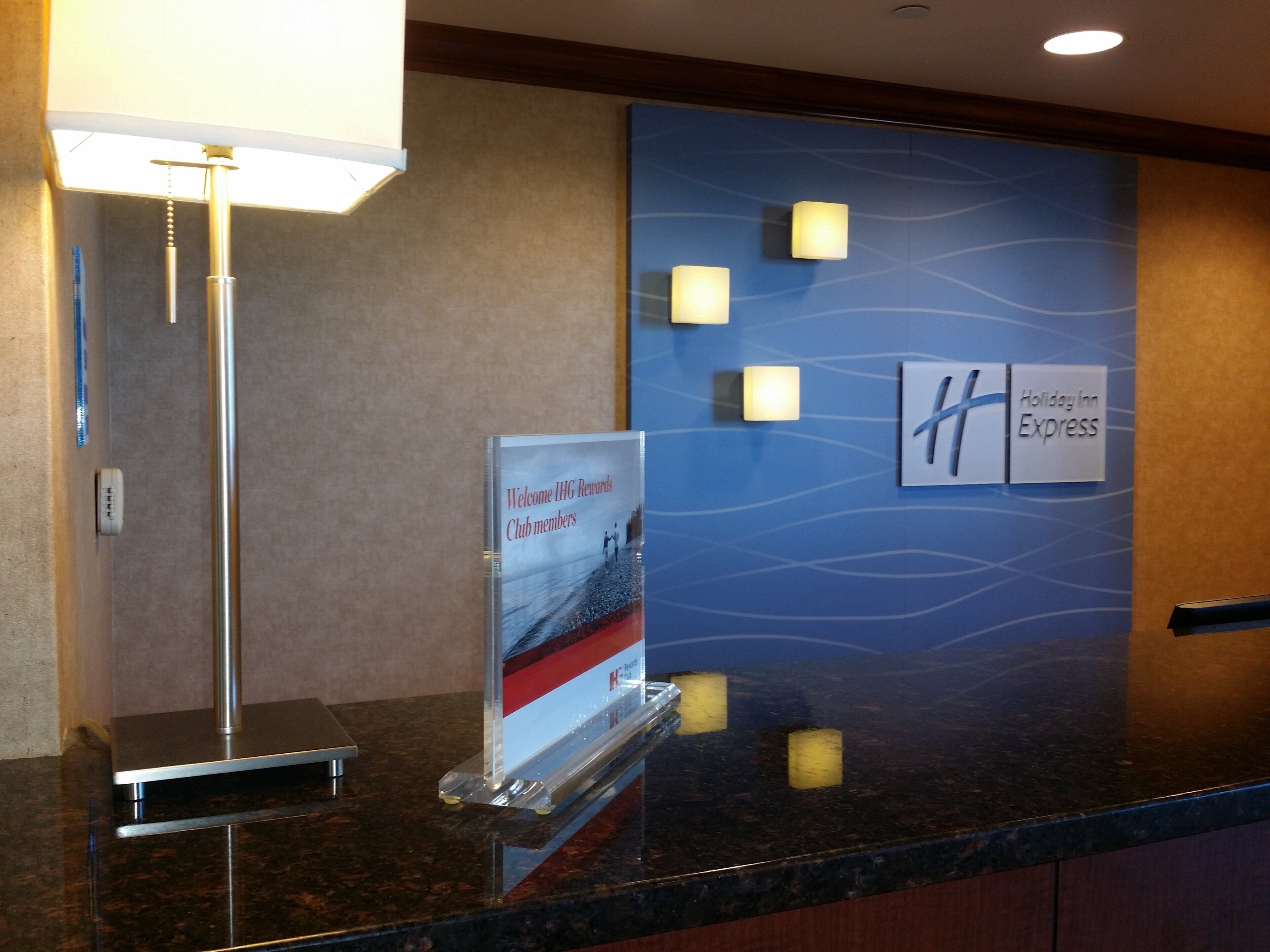 Uma mesa de recepção com parede azul, placa para membros do IHG Rewards Club e placa da Holiday Inn Express.