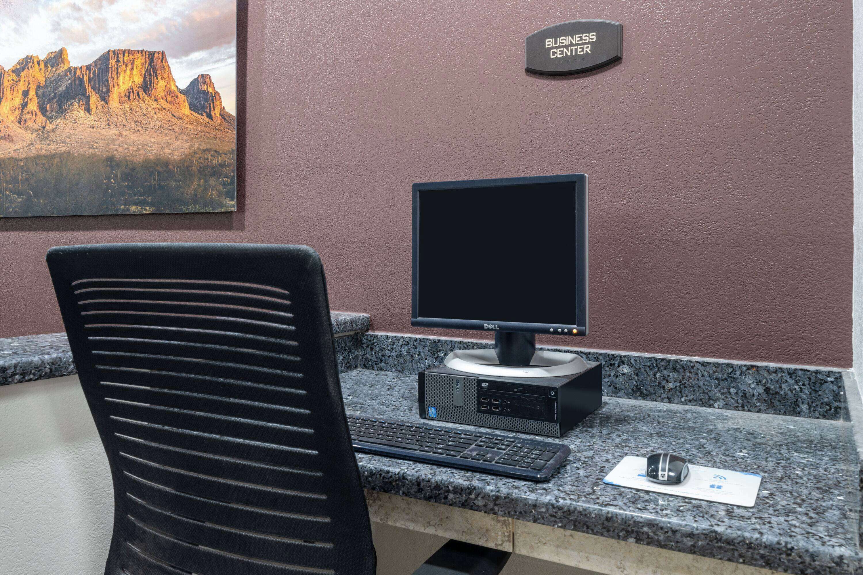 Mesa de centro de negócios com computador, teclado e rato, uma cadeira, e uma pintura com vista para as montanhas na parede.