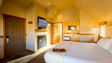 Quarto de hotel com cama, televisão, lareira e pequena mesa com computador.