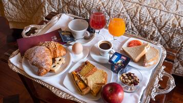 Uma bandeja de café da manhã com croissants, torradas, uma maçã, um copo de suco de laranja, um copo de suco vermelho, uma xícara de café e um pequeno recipiente com nozes.