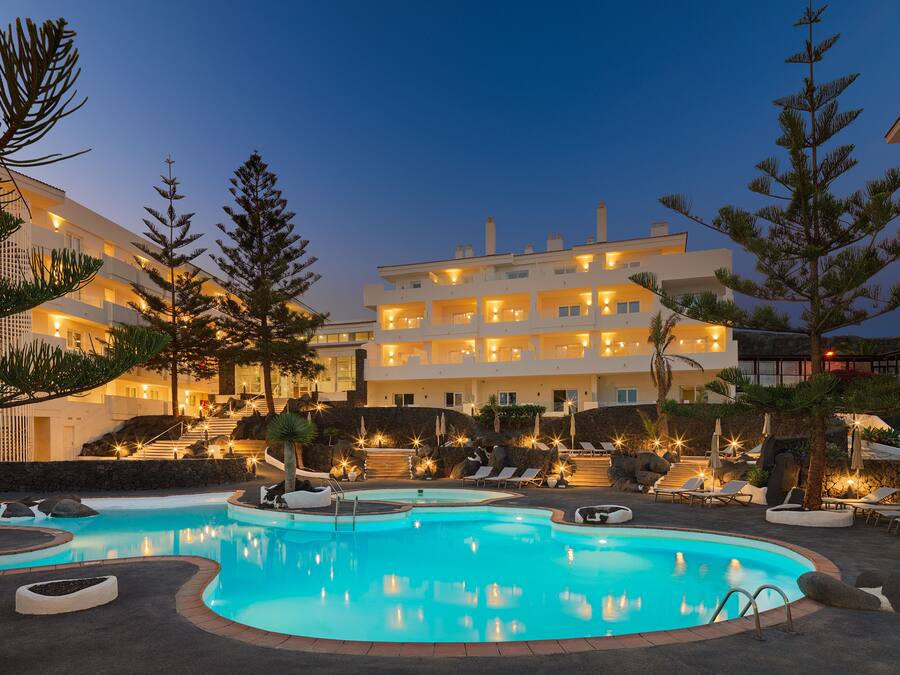 Piscina com espreguiçadeiras e um edifício ao fundo com várias varandas.