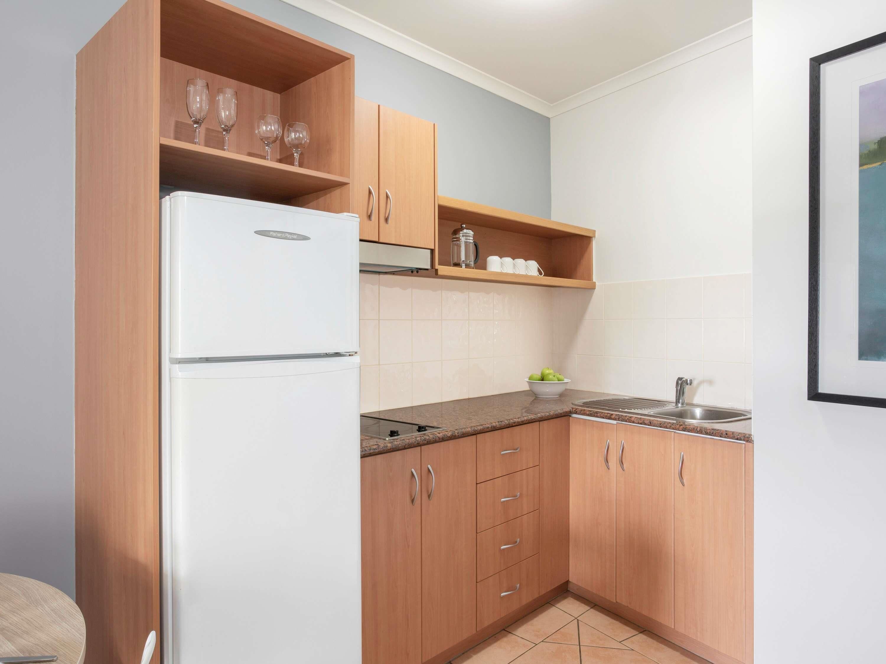Uma cozinha compacta com geladeira branca, armários de madeira, bancada e pia.