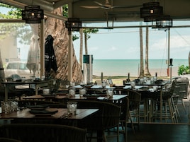 Restaurante com área externa e mesas voltadas para o mar, com móveis de vime e luminárias pendentes.