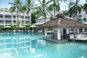 Uma área de piscina com bar, espreguiçadeiras e um pavilhão com telhado de palha.
