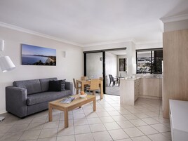 Uma sala de estar moderna com um sofá cinzento, uma mesa de centro de madeira e um espaço de jantar com mesa e cadeiras.