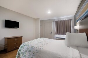 Quarto de hotel com cama, cômoda, televisão fixada na parede e janela com cortinas.
