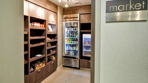 Um corredor com prateleiras de madeira repletas de lanches e bebidas, um refrigerador e uma placa com a inscrição "The Market".