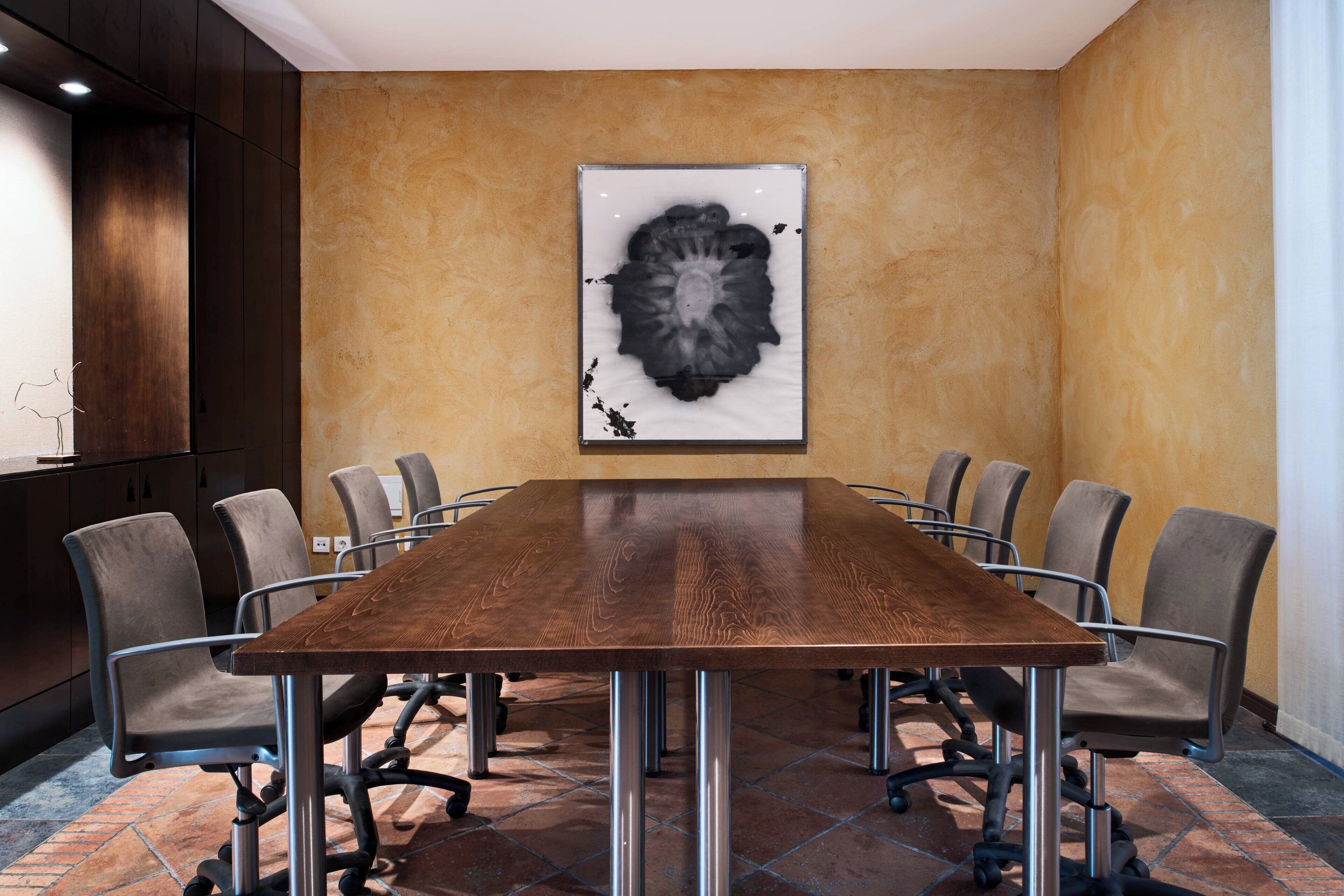 Uma sala de conferências com uma grande mesa de madeira, oito cadeiras e um quadro abstrato de grandes dimensões na parede.
