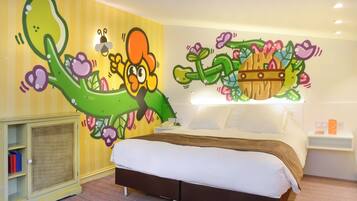 Quarto de hotel com cama, mesa de cabeceira pequena, nicho, parede com murais coloridos e um móvel para guardar objetos.