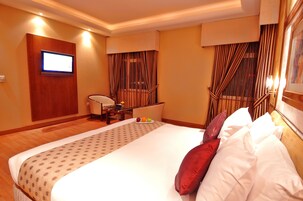 Quarto de hotel com uma cama, uma televisão fixada na parede, uma escrivaninha com cadeira e uma janela com cortinas.