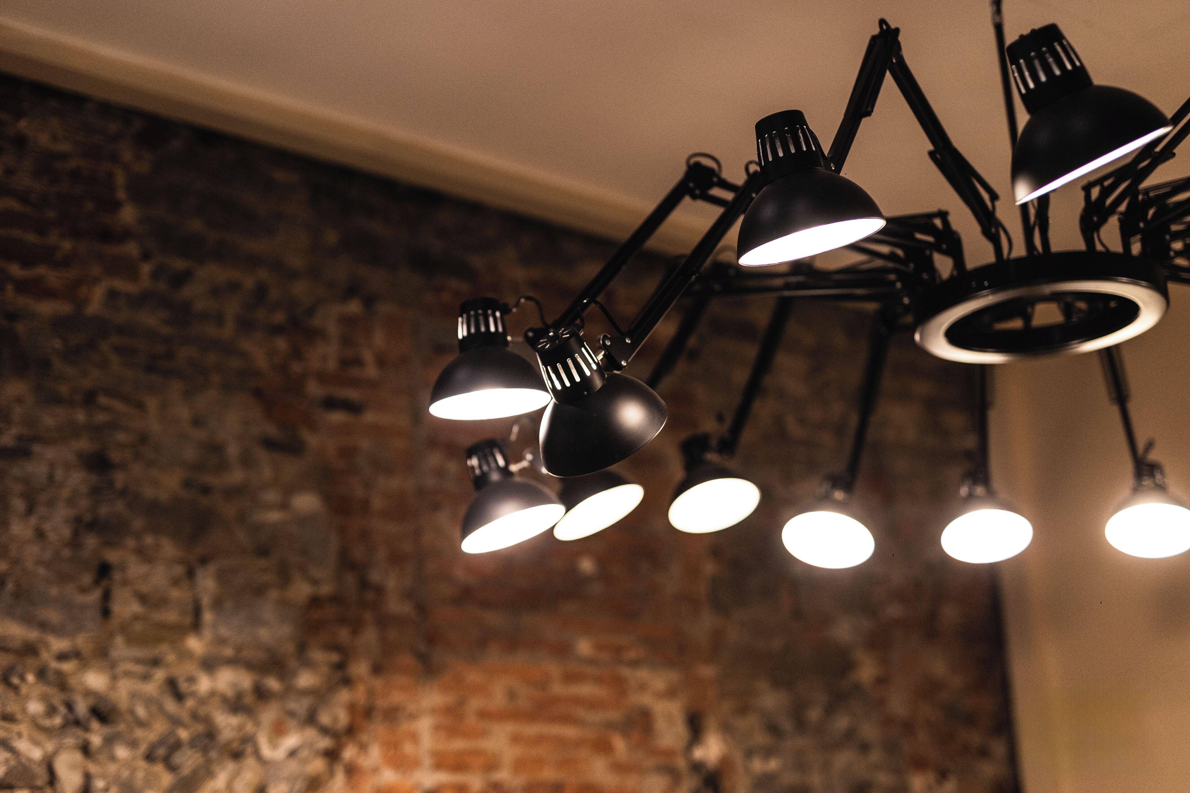 Teto com várias luminárias pendentes pretas em frente a uma parede de tijolos.