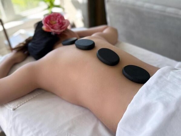 Uma pessoa recebendo massagem nas costas com pedras pretas.