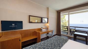 Quarto de hotel com cama, escrivaninha, cadeira, televisão, espelho e varanda com vista para o mar.