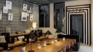 Um saguão de hotel moderno com um longo balcão de recepção de madeira, luminárias pretas e uma parede decorada com obras de arte emolduradas.