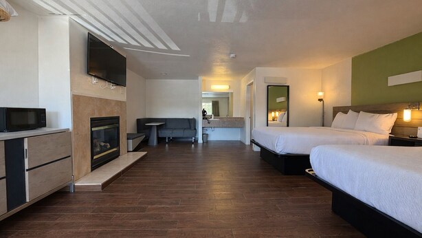 Quarto de hotel com cozinha compacta, lareira, televisão, cama e banheiro ao fundo.