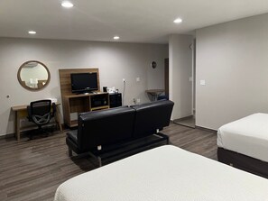 Quarto de hotel com cama, escrivaninha e cadeira, televisão, micro-ondas e uma pequena mesa com abajur.