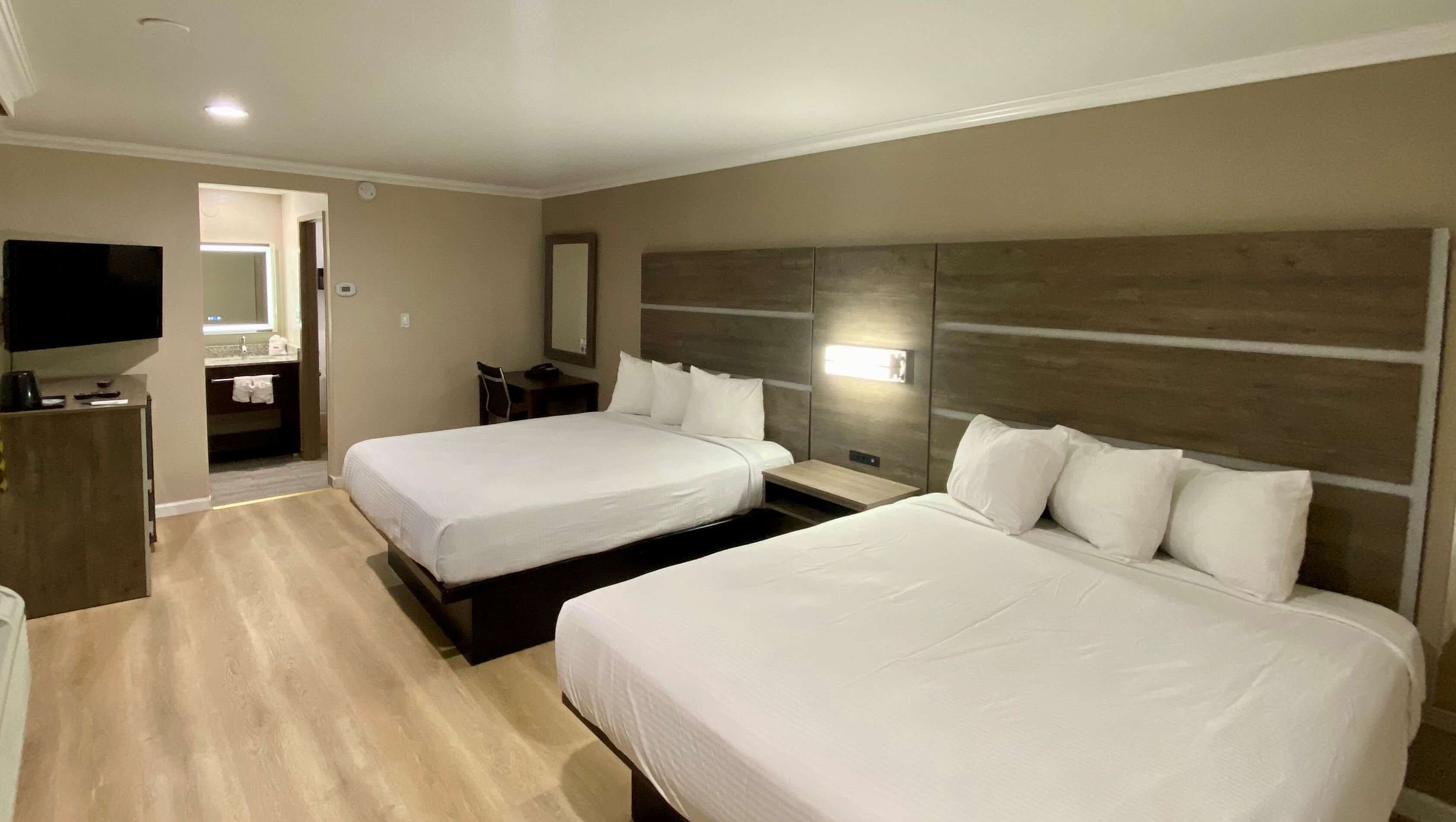 Quarto de hotel com duas camas, televisão, escrivaninha e banheiro.