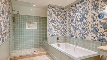 Casa de banho com chuveiro, banheira e azulejos com padrão floral.