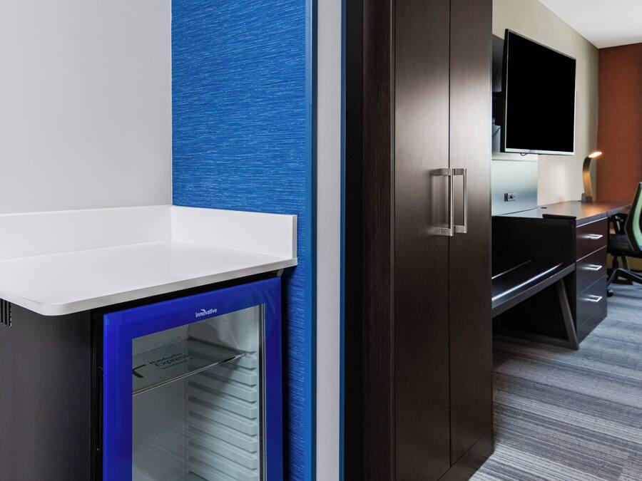 Um espaço de escritório moderno com uma parede azul de destaque, uma mesa branca, um computador e uma TV fixada na parede.
